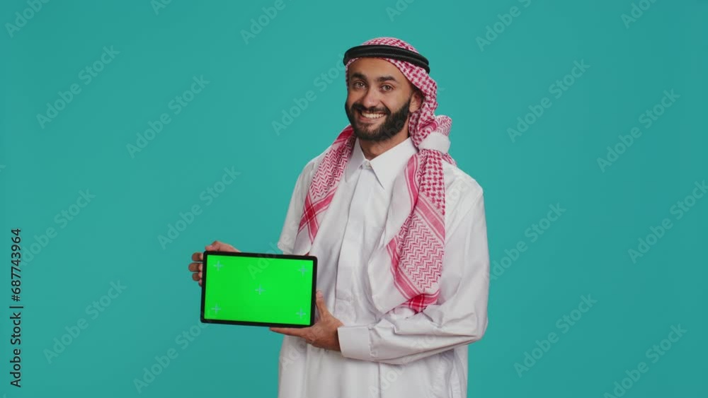 Muslim man presents greenscreen tablet over blue background, showing ...