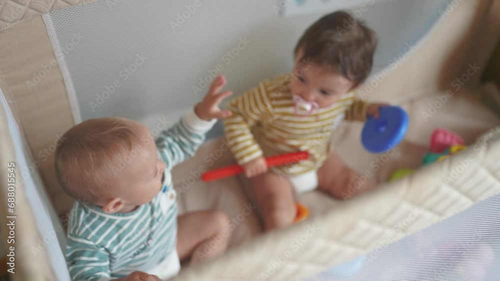 baby twins fight sitting in crib playpen. two baby toddlers are sitting ...