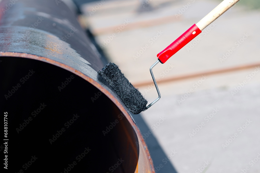 Metal pipe is painted with paint roller with black paint or bitumen ...