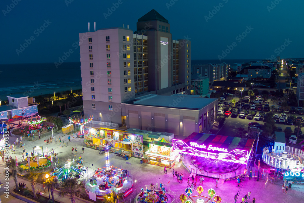 aerial shot of the Carolina Beach Boardwalk with ocean water, people on the beach, hotels and ...