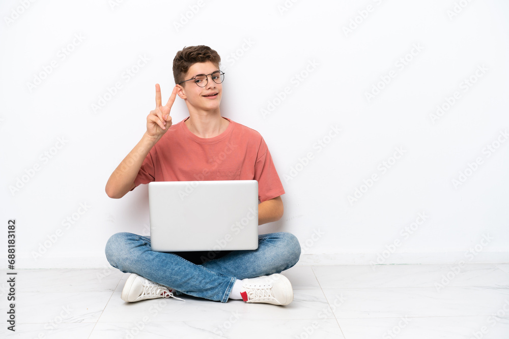 Teenager Russian man holding pc sitting on the floor isolated on white ...