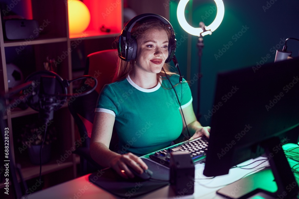 Young redhead woman streamer playing video game using computer at ...