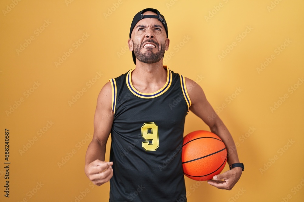 Middle age bald man holding basketball ball over yellow background ...