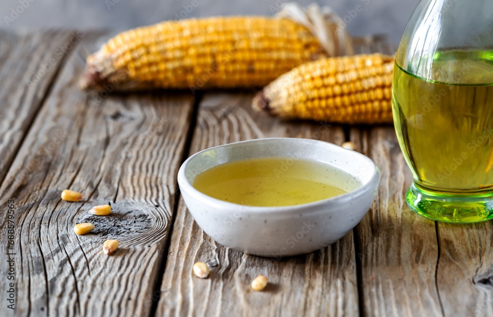 Corn oil in ceramic bowl, corn cobs and oil jug over rustic wooden ...