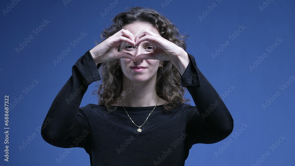 Woman doing heart shape with hands standing on blue background looking ...