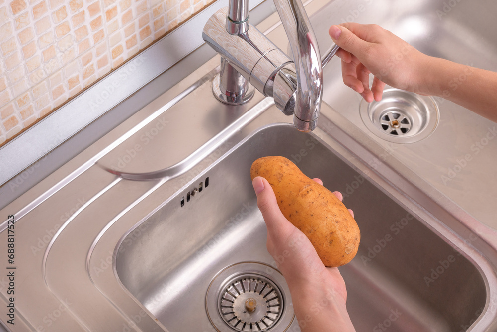 Female hands washing potato with hand under running water in sink in ...