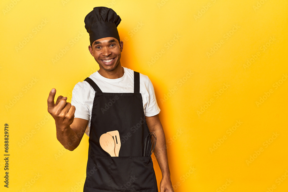 African American cook with utensils, yellow studio, pointing with ...