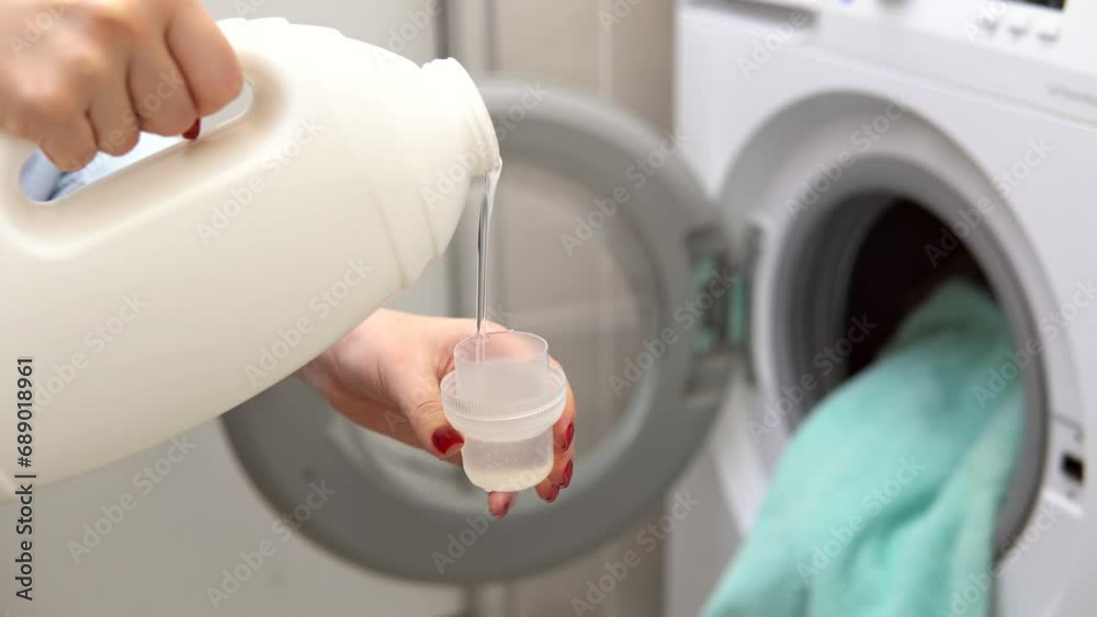 Woman pouring liquid washing gel softener from bottle into cap for ...