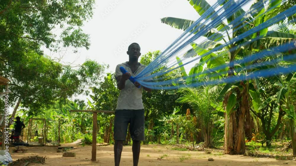 Poor black man rolling up a blue Kente cloth in a tropical village in ...