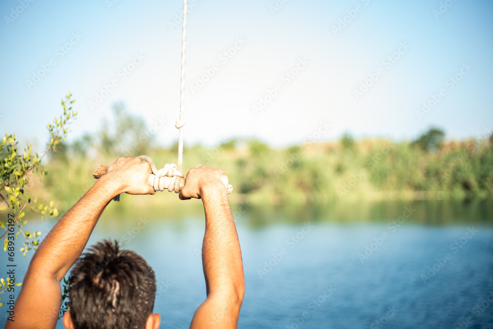 Detail of hands of young Caucasian man grabbing a stick and a rope tied ...