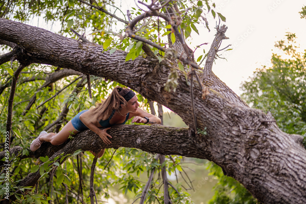 An active and fit girl uses a tree in a park to warm up and train ...