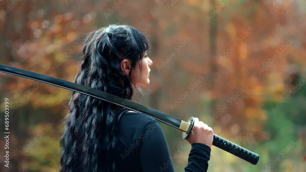 Beautiful girl with long hair in a black outfit holds a Japanese katana ...
