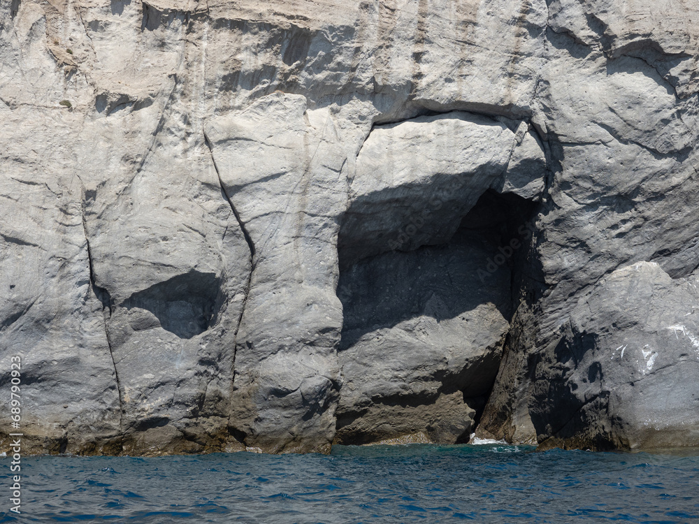 Weathered seaside rock face texture with blue water. Aged volcanic ...