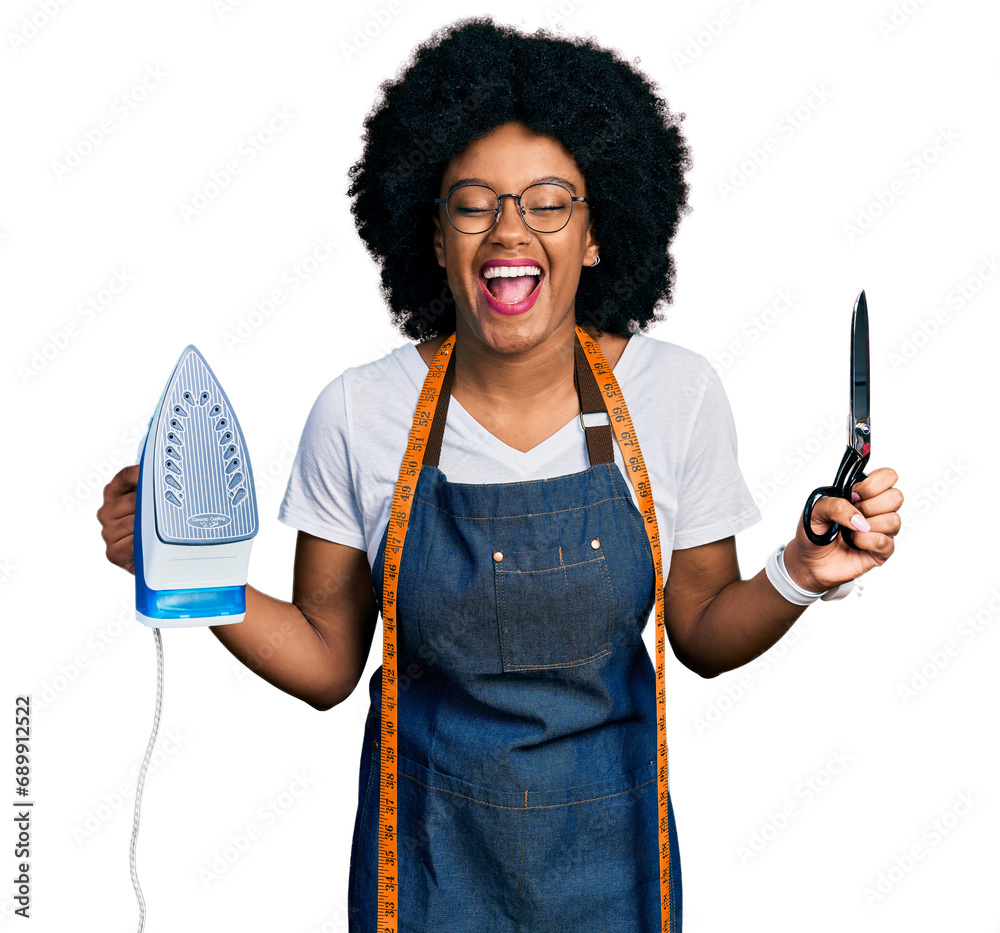 Young african american woman dressmaker designer wearing atelier apron holding iron and scissors ...