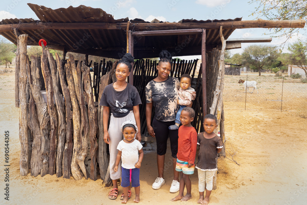 village, african family sited in front of the outdoors kitchen shack in the yard, mother with ...