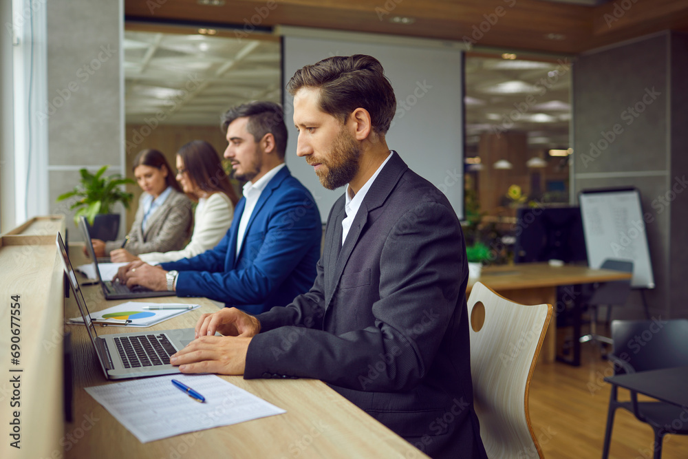 Serious business people sitting in a row and working on laptop in ...