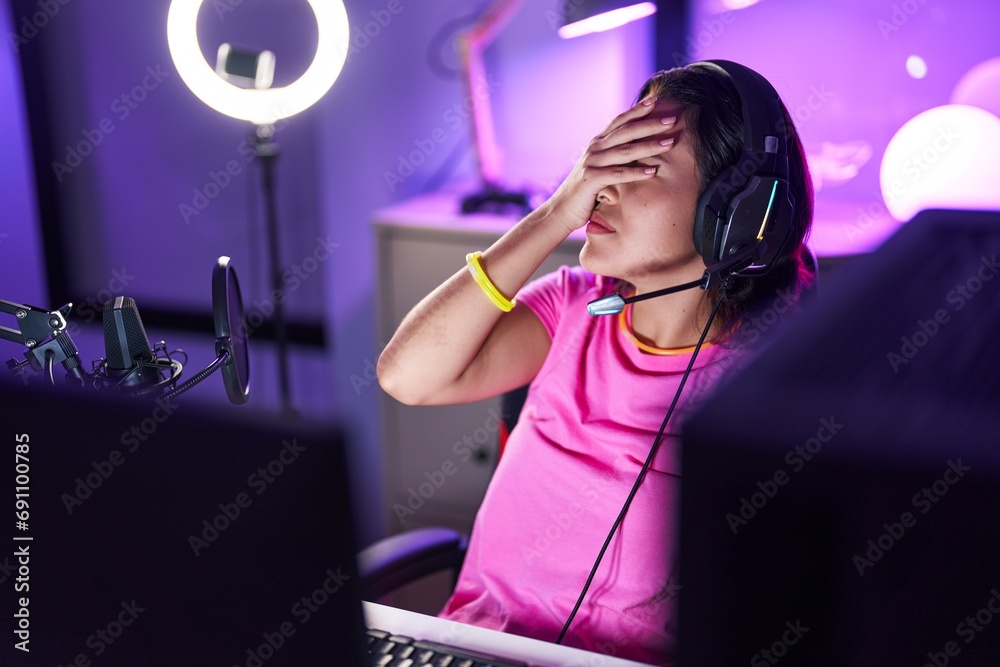 Young hispanic woman streamer stressed using computer at gaming room ...