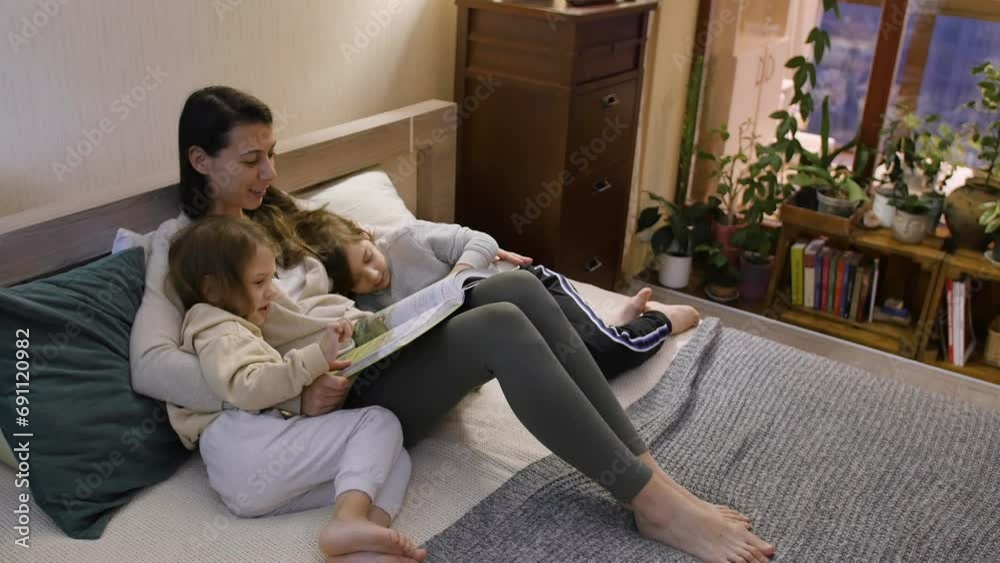 Mom is lying on the bed with her children, reading a bedtime story. Her ...