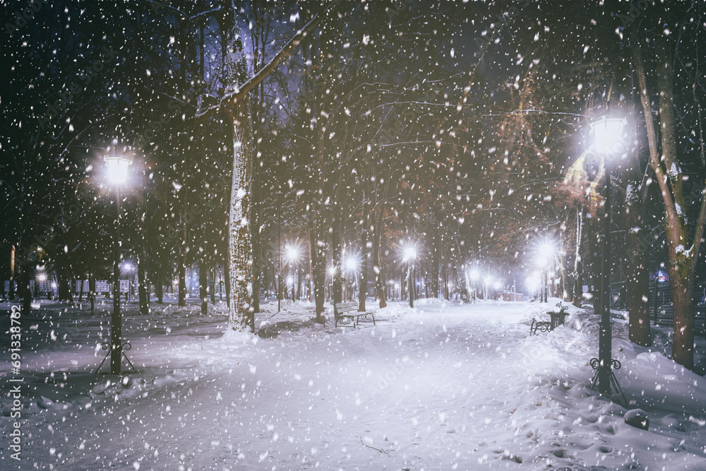 Snowfall in a winter park at night with glowing lanterns, pavement ...