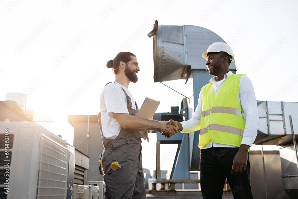 Smiling bearded worker in overalls standing and holding modern tablet ...