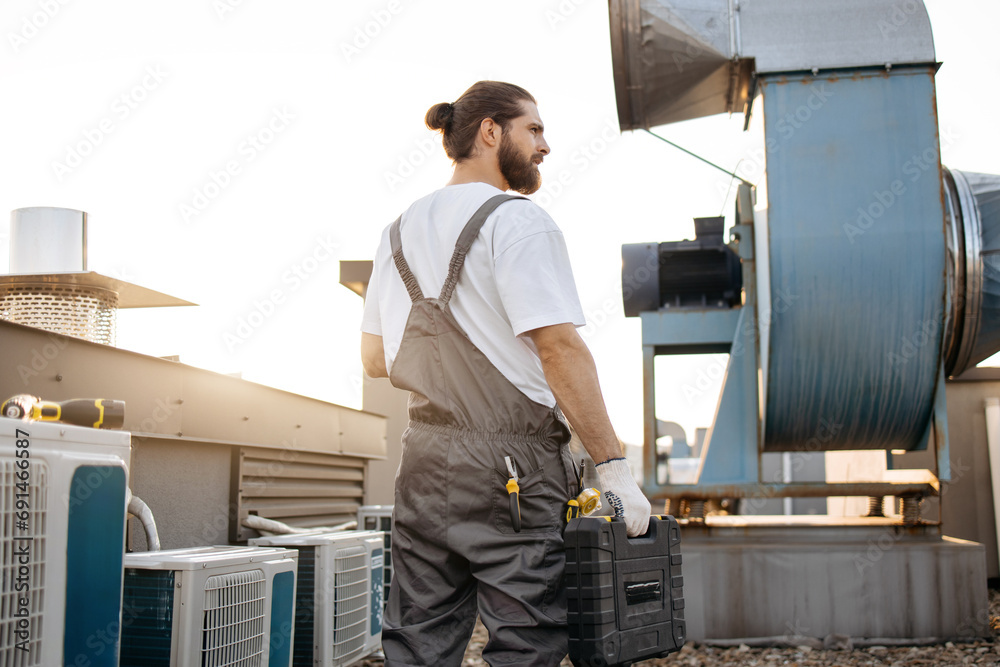 Back view of stocky bearded master dressed in overalls standing and ...