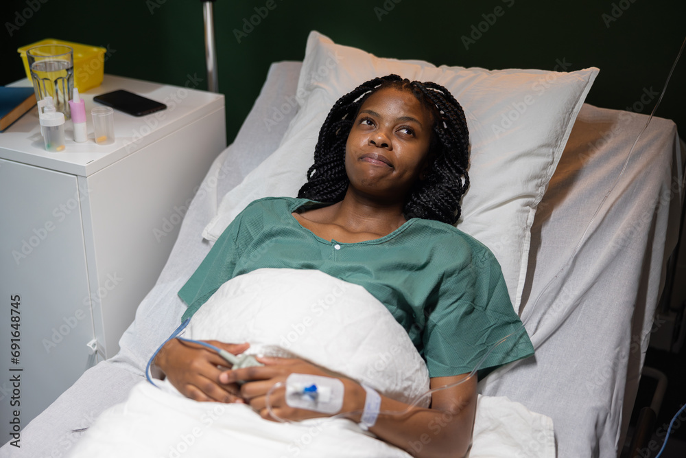 African woman lies in her hospital bed, calmly looking at the camera ...
