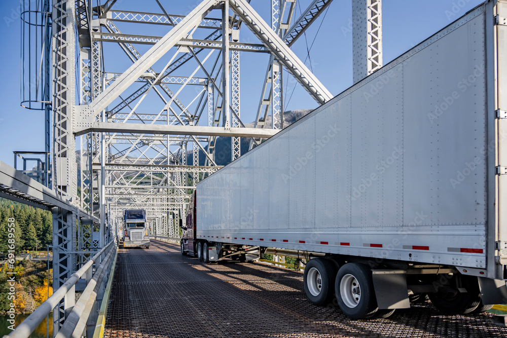 Two industrial big rig semi trucks with loaded semi trailers moving ...