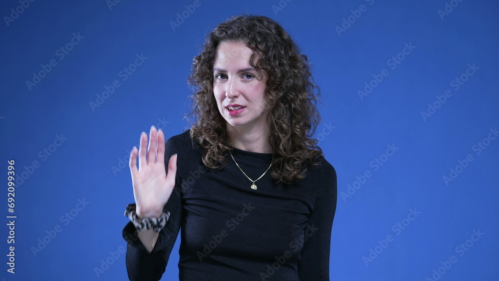 Shy woman saying hello to viewer with hands standing on blue background ...