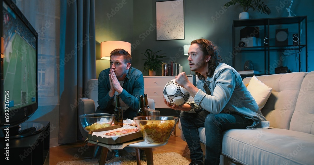 Two male best friends cheering for football team in dark living room ...