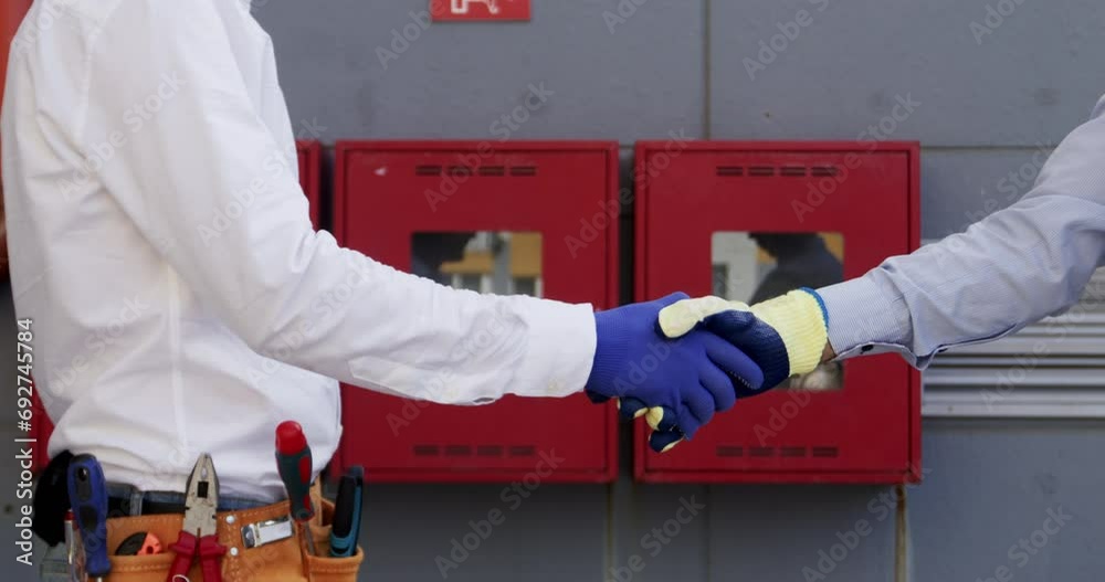 Workers shake hands standing against fire safety boxes at construction ...