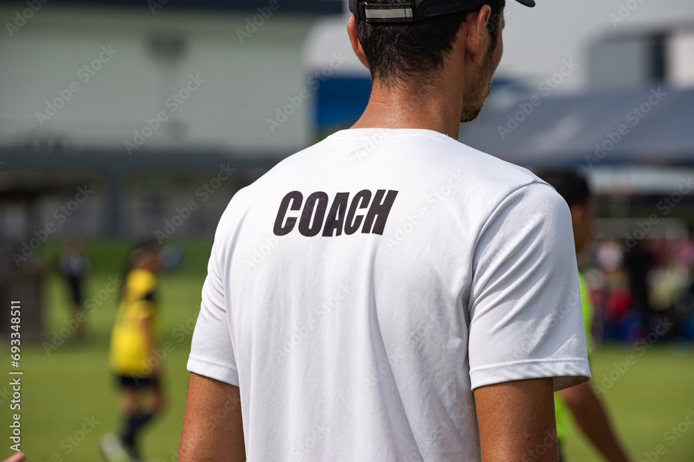 Male youth football coach standing and watching his team playing in a ...