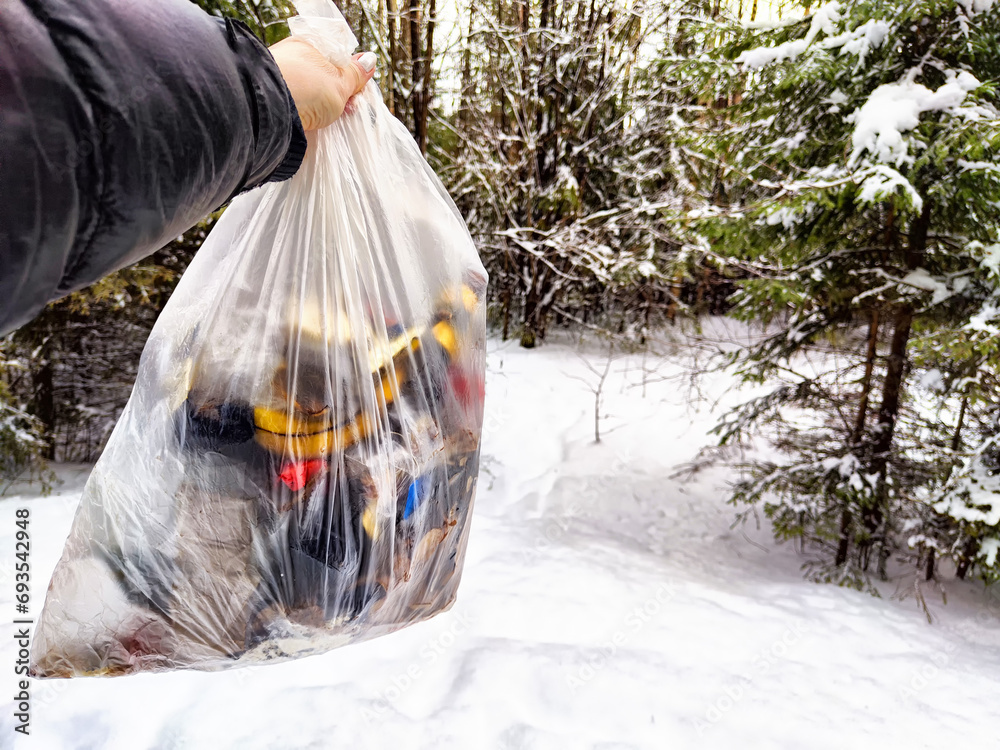Bag of garbage in hand of woman and snow in forest on the background. A ...
