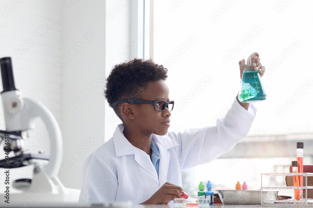 Concentrate African boy in lab coat holds chemical flask for doing ...