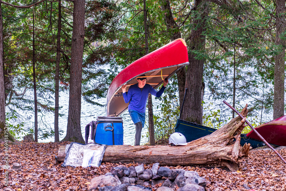 Canoe tripping: a young man shoulder carries a red canoe from the water ...