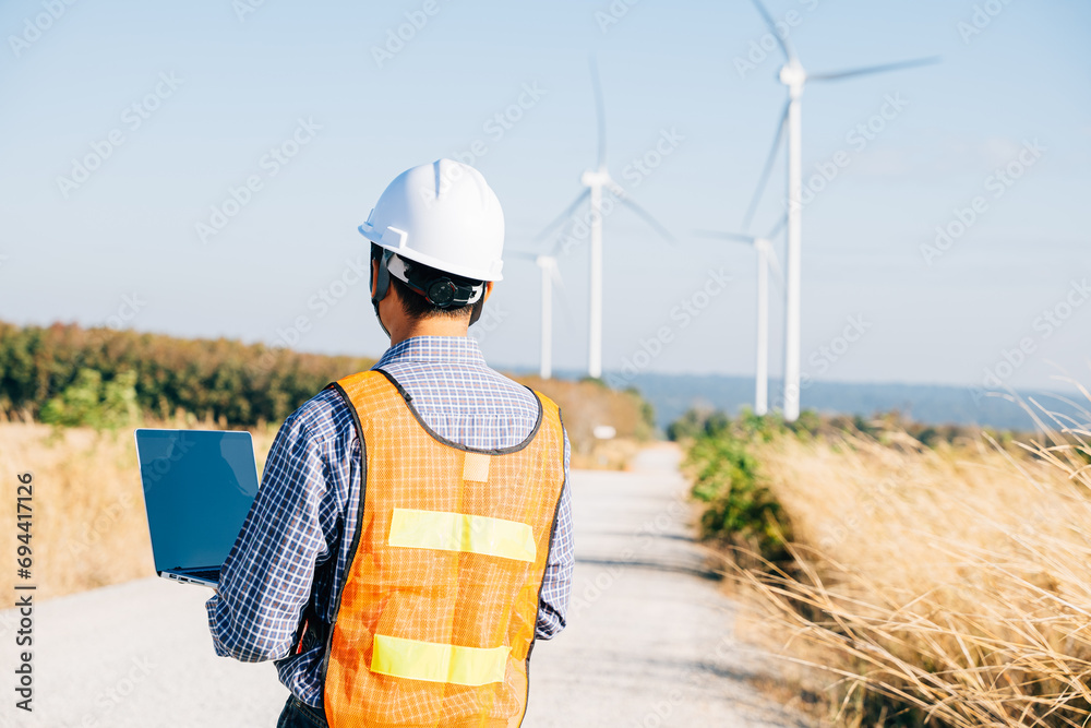 Engineer with laptop by wind turbines. Service technician ensuring ...