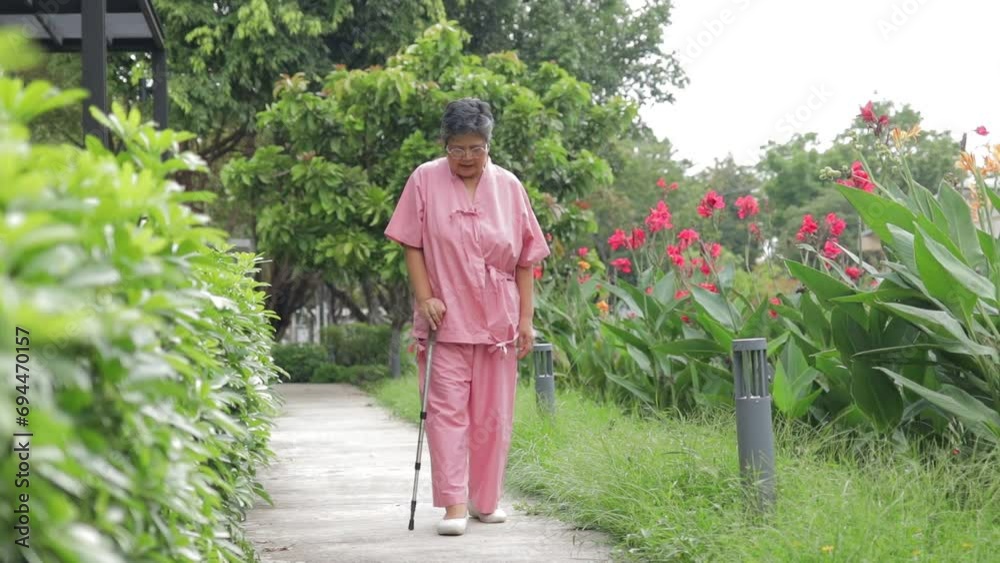An elderly Asian female patient walks using a cane to support herself ...