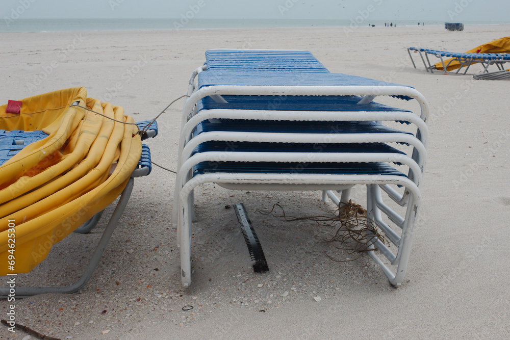 Yellow and Blue beach chairs and canopy's stacked in middle with sand ...