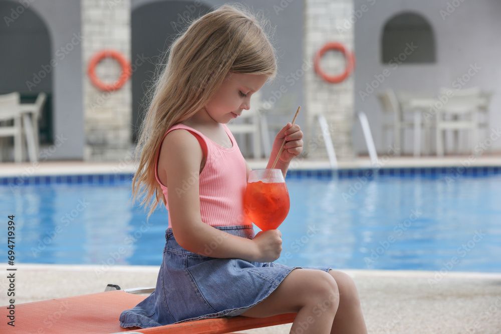 Adorable little girl having refreshment drinkby the poolside ...