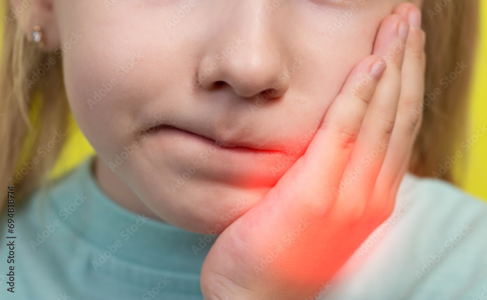 A little girl holds her hand on her sore cheek and has a toothache. The concept of malocclusion ...