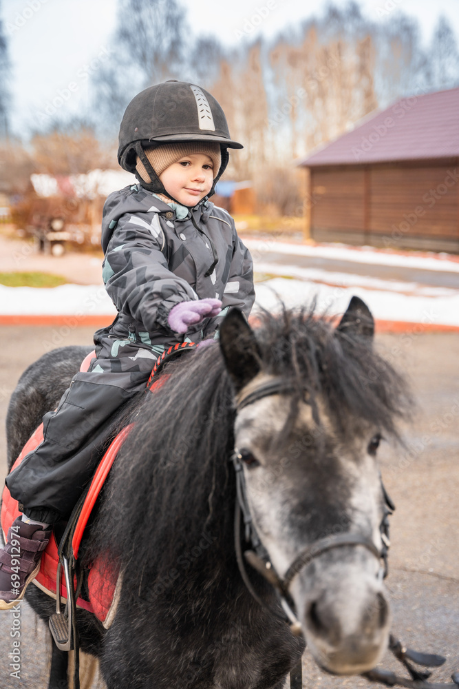 Little cute girl riding a little horse or pony in the winter in field ...