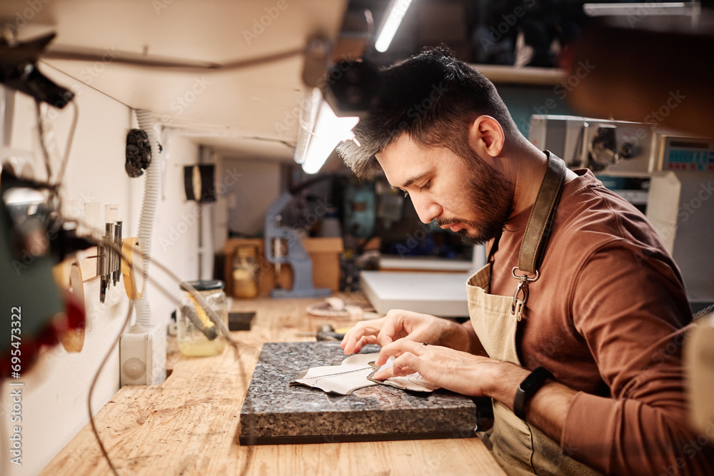 Side view of young Asian male shoemaker creating patterns for footwear ...