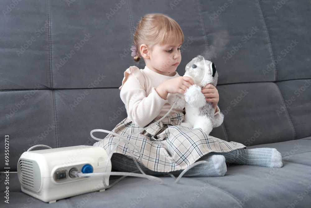 A little bright girl treats her soft toys with a nebulizer inhaler ...
