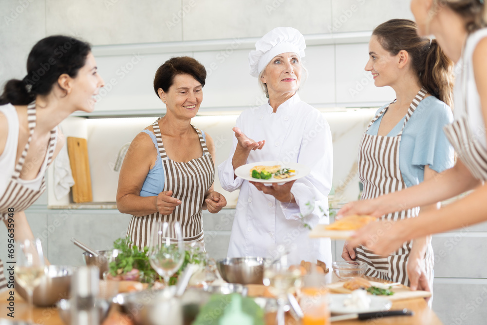 Elderly woman cook shows group prepared chicken dish at cooking master ...