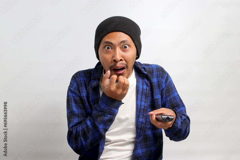 Scared Asian man, adorned in beanie hat and casual shirt, holds TV ...