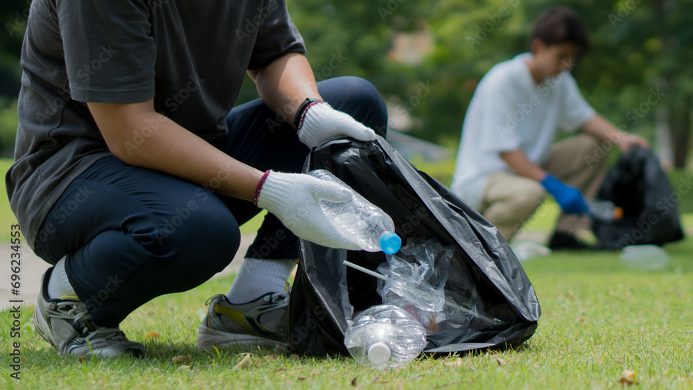 Man's hand collecting plastic waste bottles into a black bag in a park ...