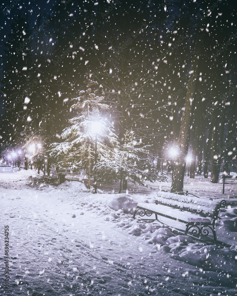 Snowfall in a winter park at night with glowing lanterns, pavement ...