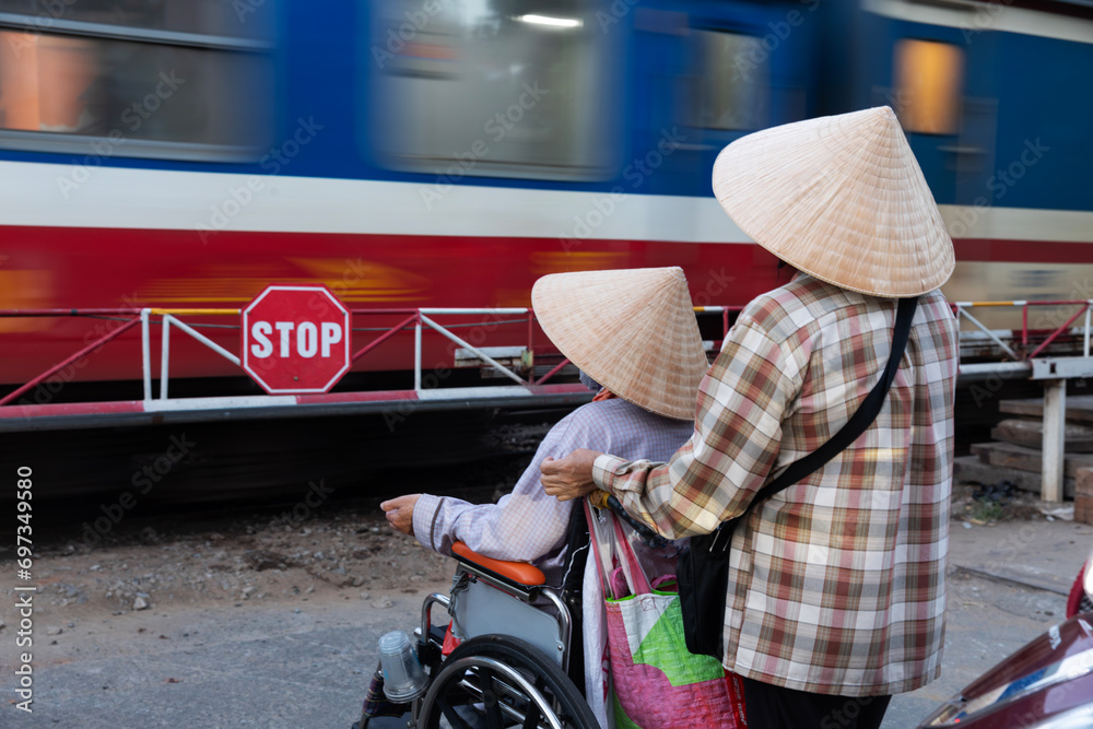 Patient in wheelchair with care worker at level railway crossing with ...