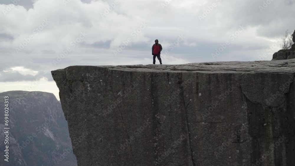 man hiker tourist standing on Preikestolen Pulpit Rock cliff and bends ... man hiker tourist standing on Preikestolen Pulpit Rock cliff and bends ...