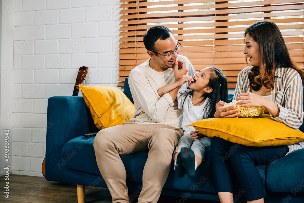 A delightful family enjoys TV and popcorn on grooved sofa fostering ...