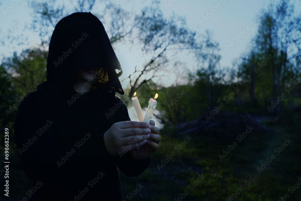 dress black witch with burning candles in hands, blurred dark nature ...